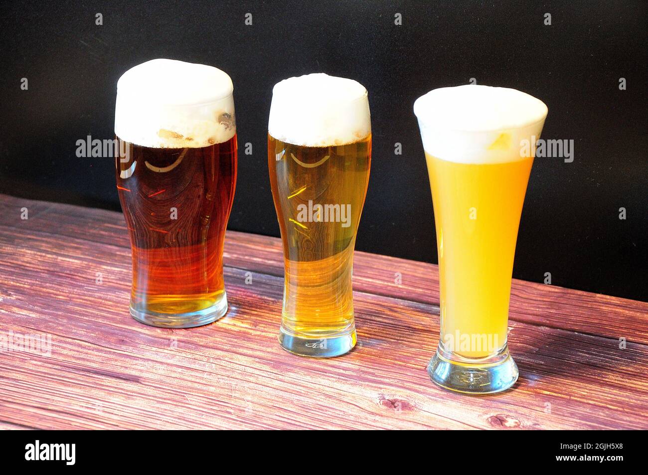 Three different glasses of light, wheat and dark beer with white foam ...