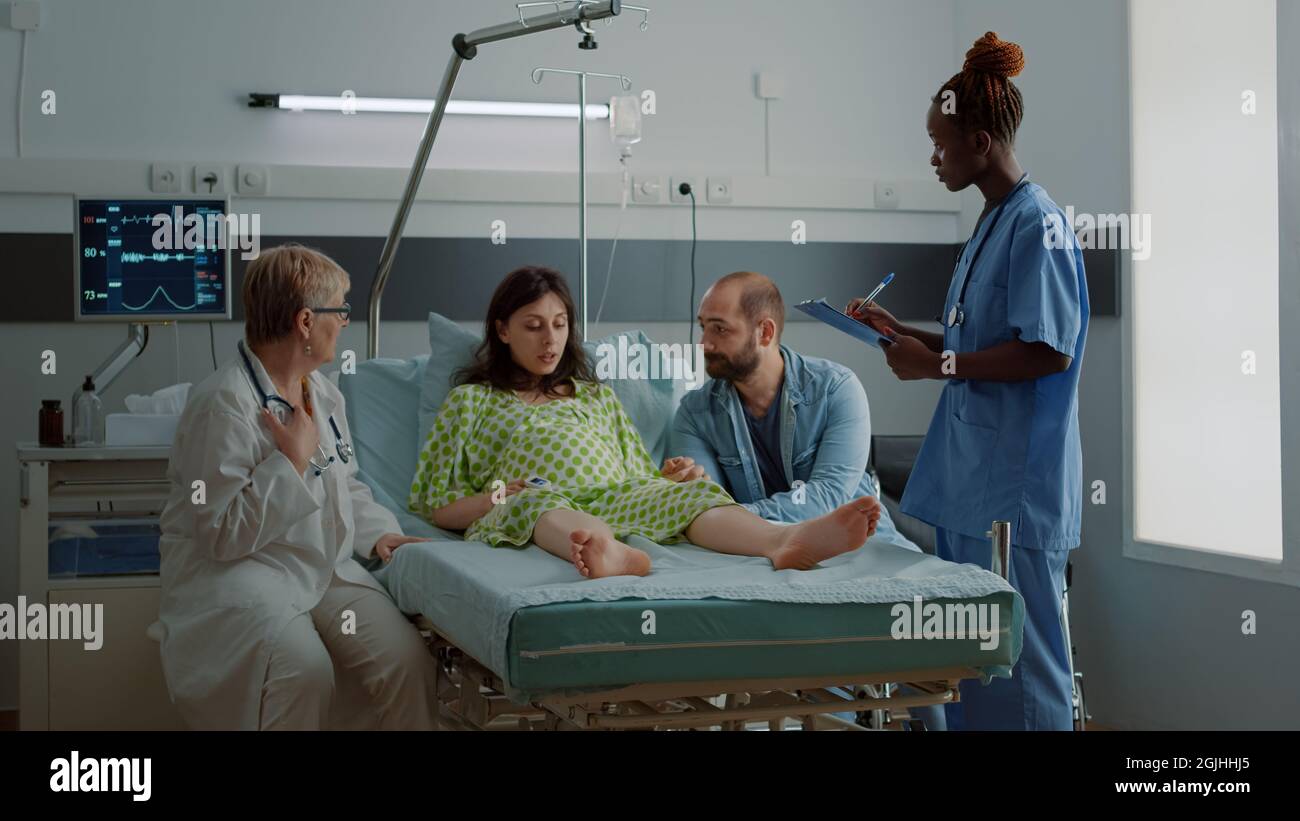 Multi Ethnic Medical Team Talking To Pregnant Woman Sitting With
