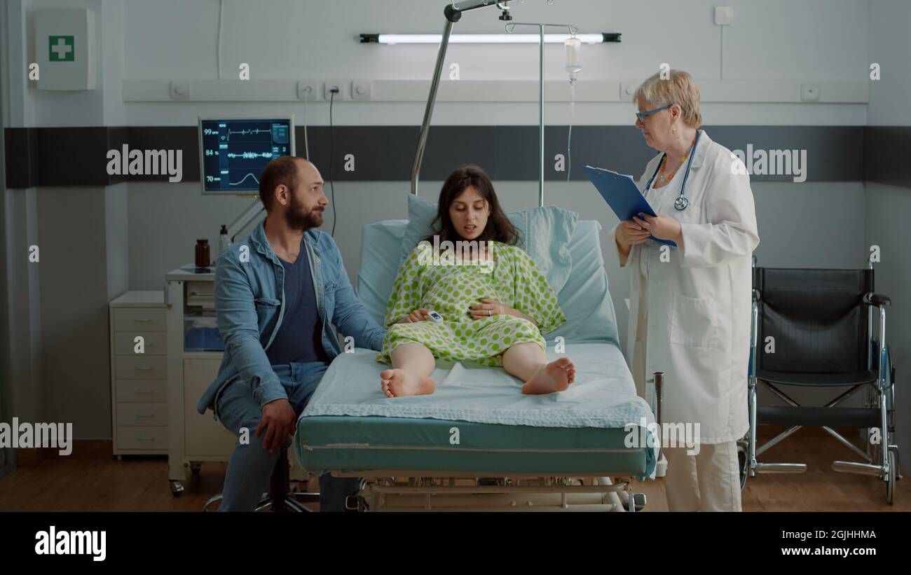 Caucasian pregnant person getting advice from doctor while sitting with ...