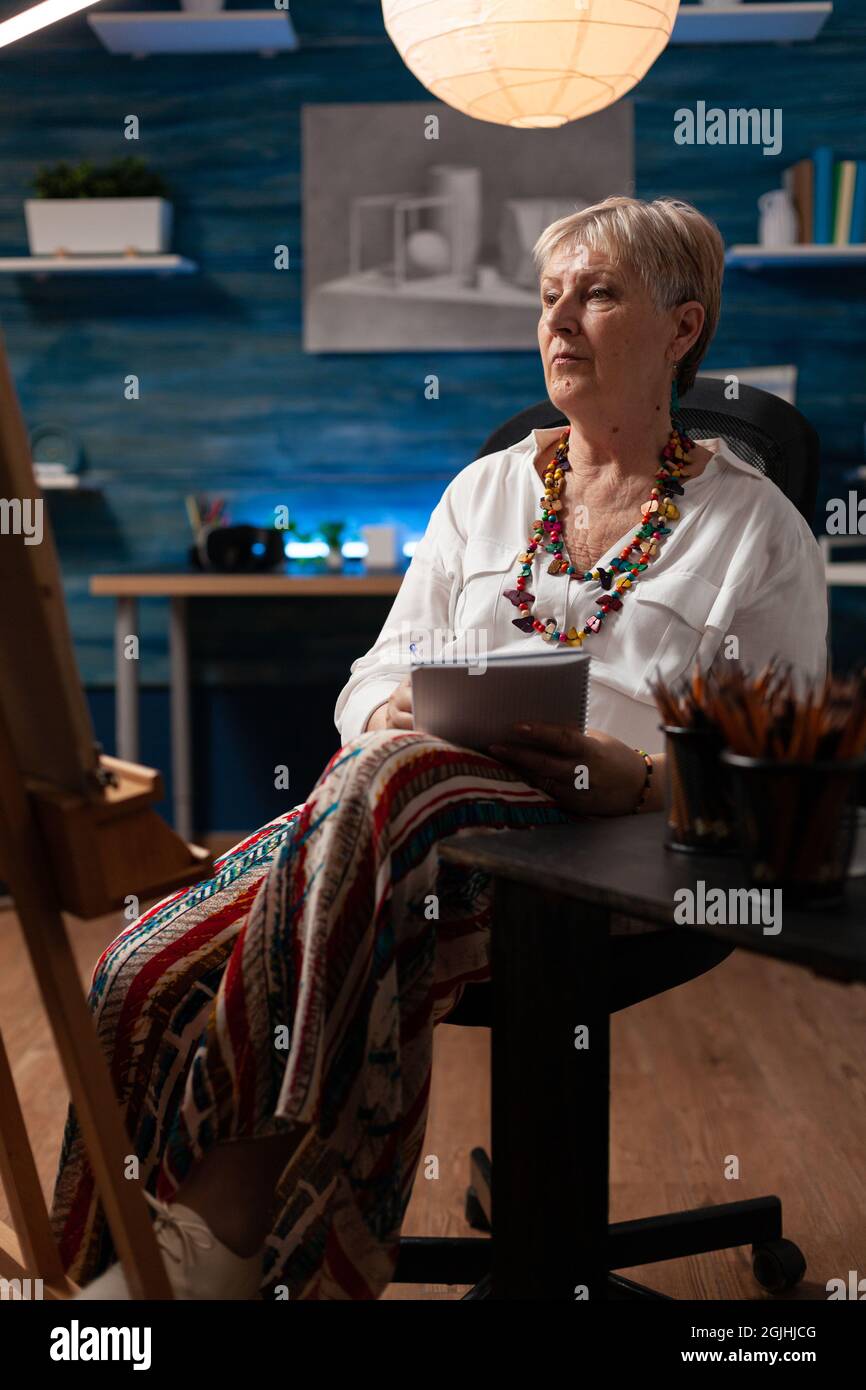 Old artist sitting in artwork studio with notebook to create sketch for ...