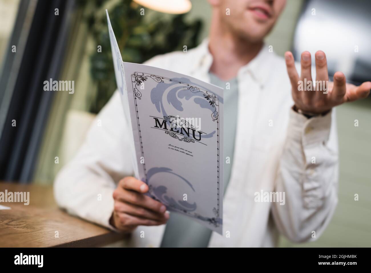 cropped view of blurred young man holding menu and gesturing in cafe ...