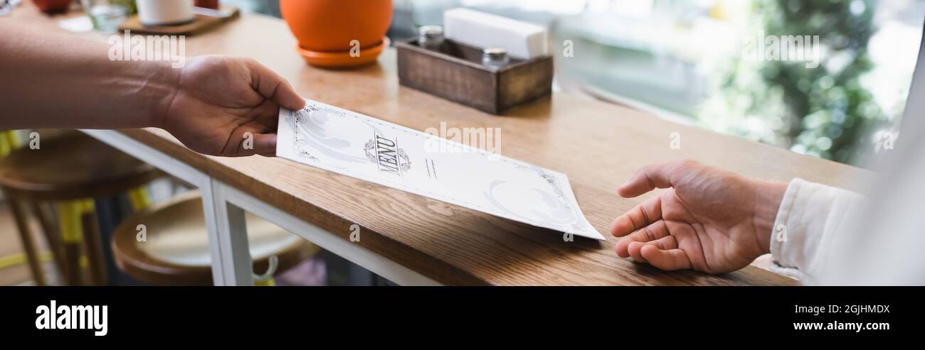 cropped view of waiter giving menu to client in cafe, banner Stock ...