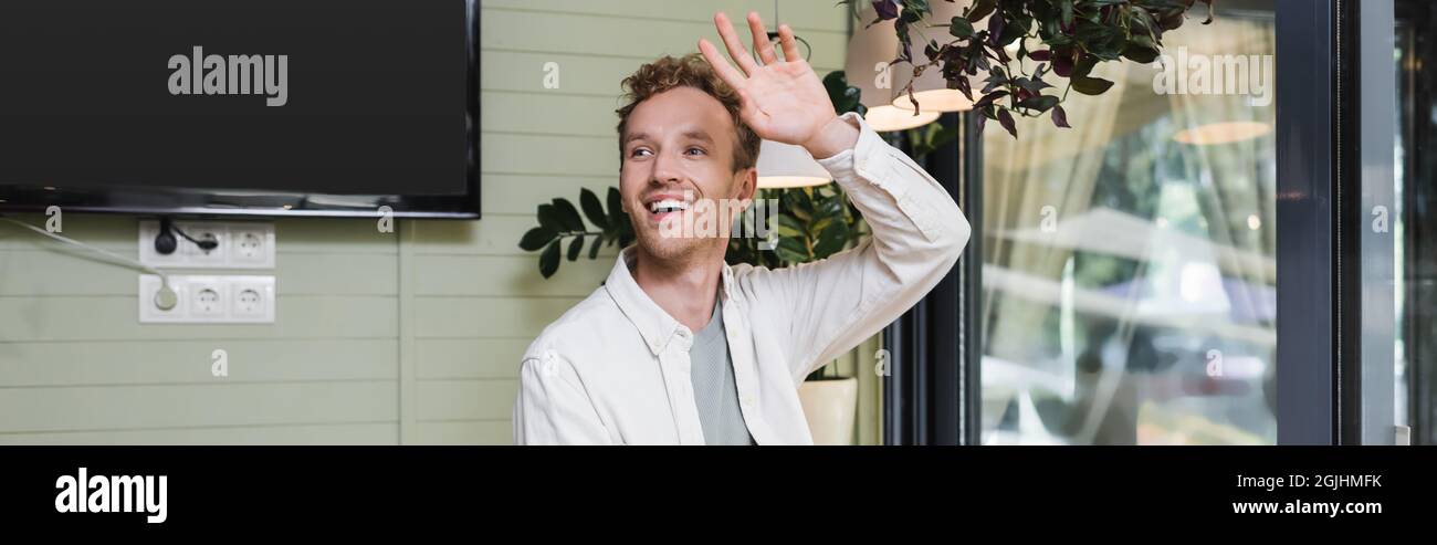 positive man waving hand and looking away in cafe, banner Stock Photo ...