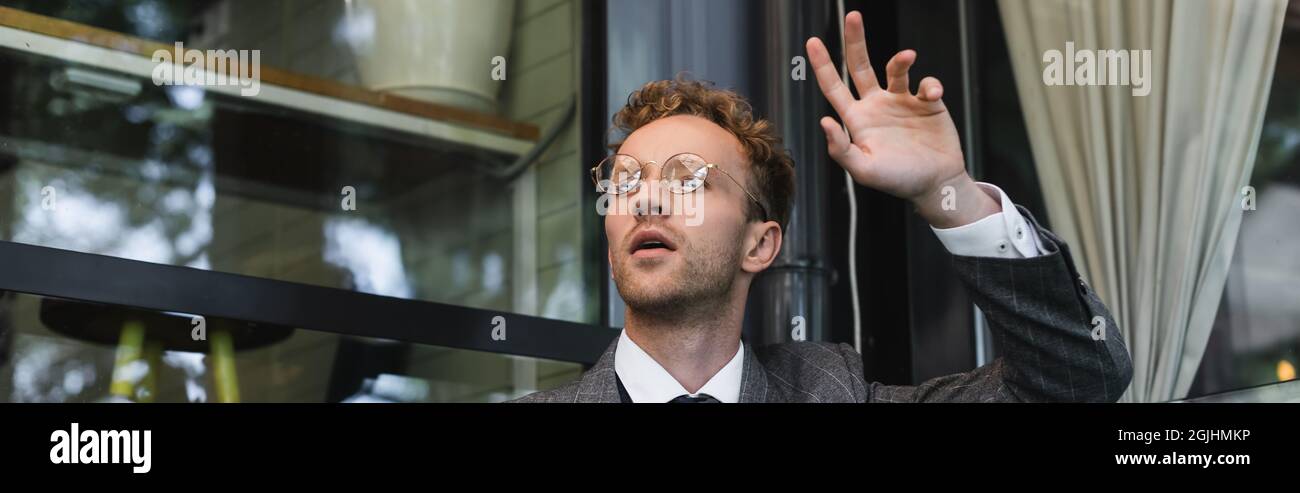 businessman in glasses with raised hand calling waiter on terrace of ...