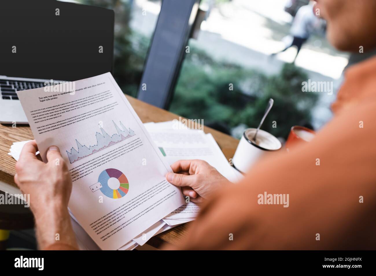 cropped view of young man holding charts and graphs near laptop in cafe ...