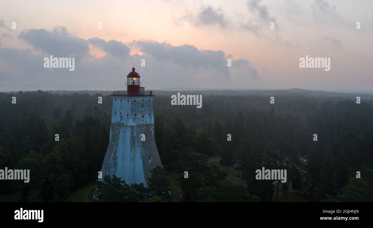 Beautiful scenery of a white beacon above green forest under red sky ...