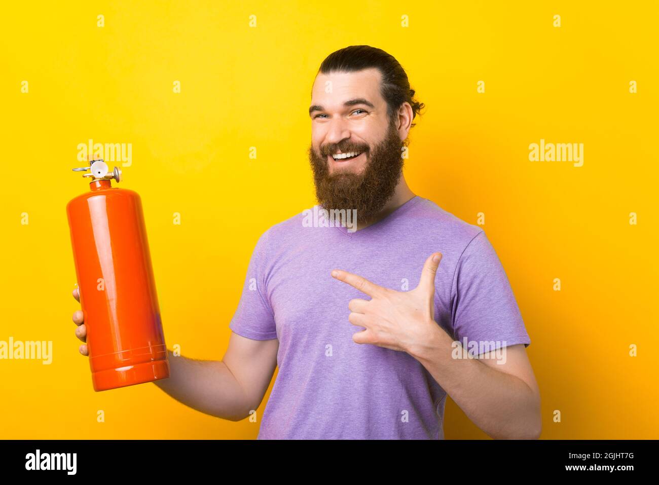 Smiling bearded man is pointing at a red fire extinguisher over yellow ...