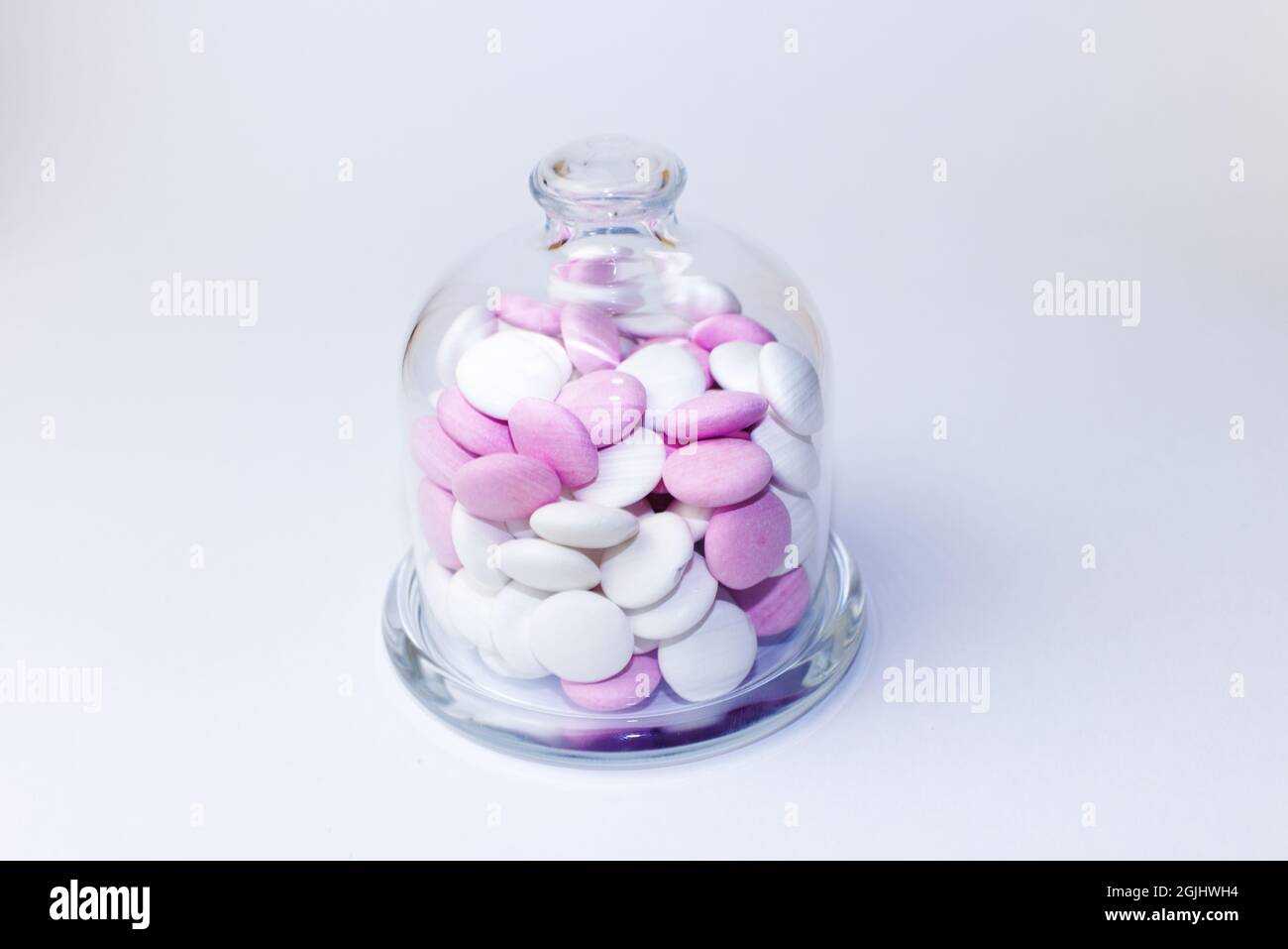 Pink and white peppermint candies in a glass jar on a white background ...