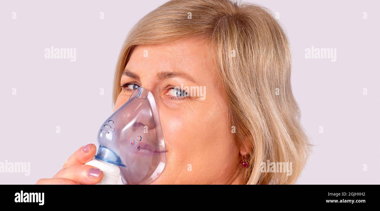 Close up photo of a blonde woman holding on her face the oxygen mask to ...