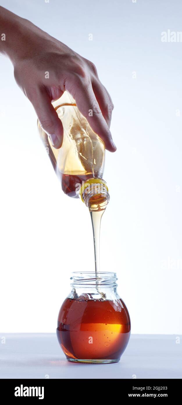 Vertical shot of a hand pouring honey from bottle to jar on white ...