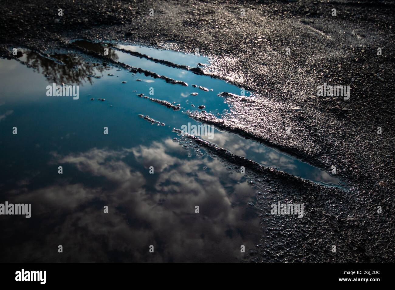 Reflection of blue sky and clouds in a big puddle with tire tracks ...