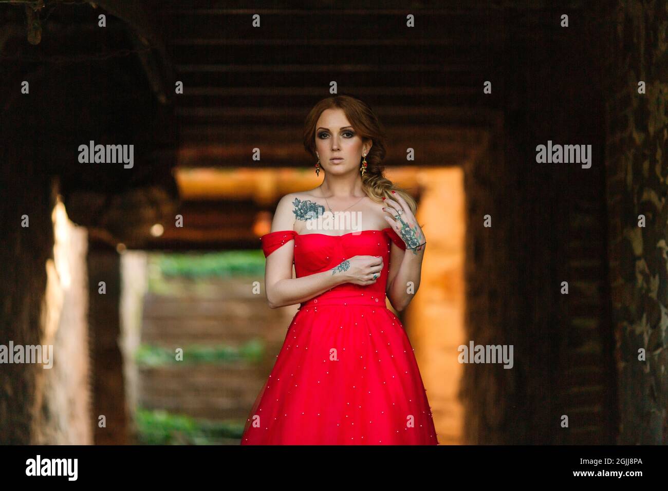 Attractive redhead tattooed woman in long red dress and diadema on ...