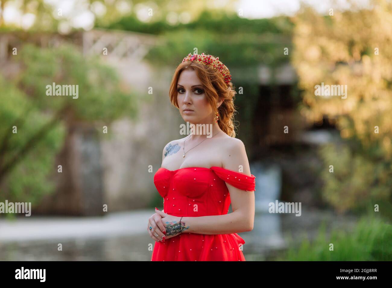 Portrait of attractive redhead tattooed woman in red dress and diadema ...
