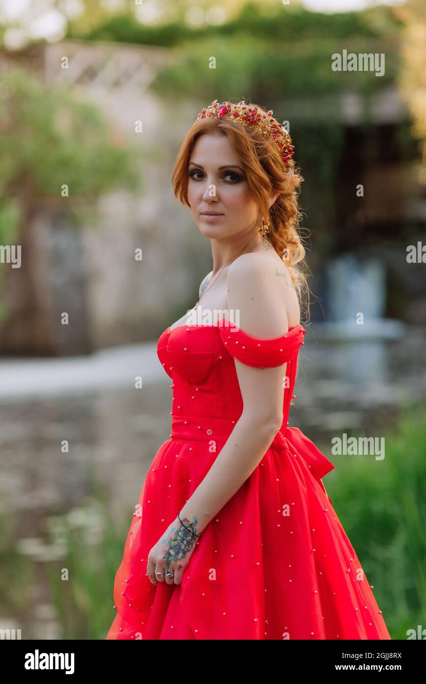 Portrait of attractive redhead tattooed woman in red dress and diadema ...