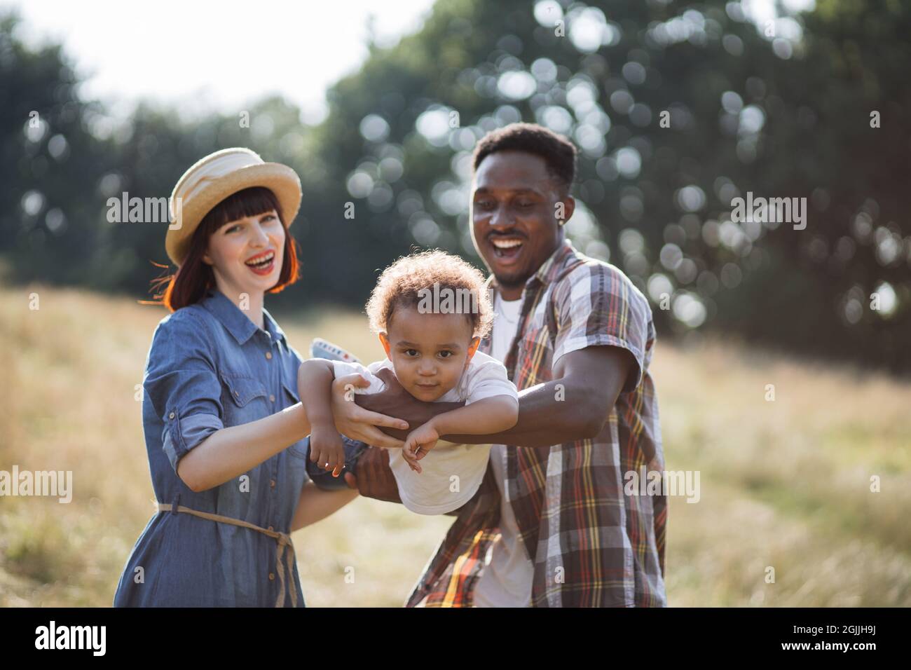 Cheerful young parents playing with lovely little son on fresh air ...