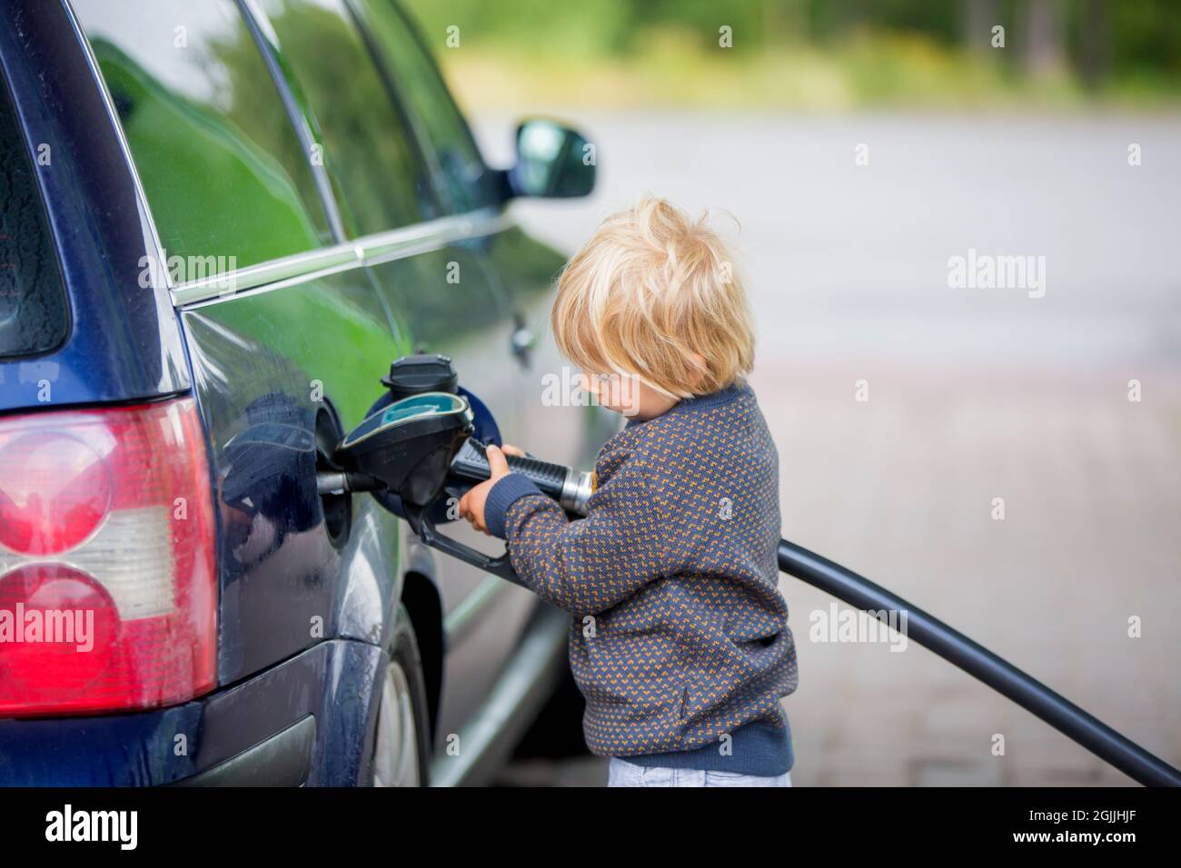 Sweet little child, blond boy, helping parents to put fuel in the car ...
