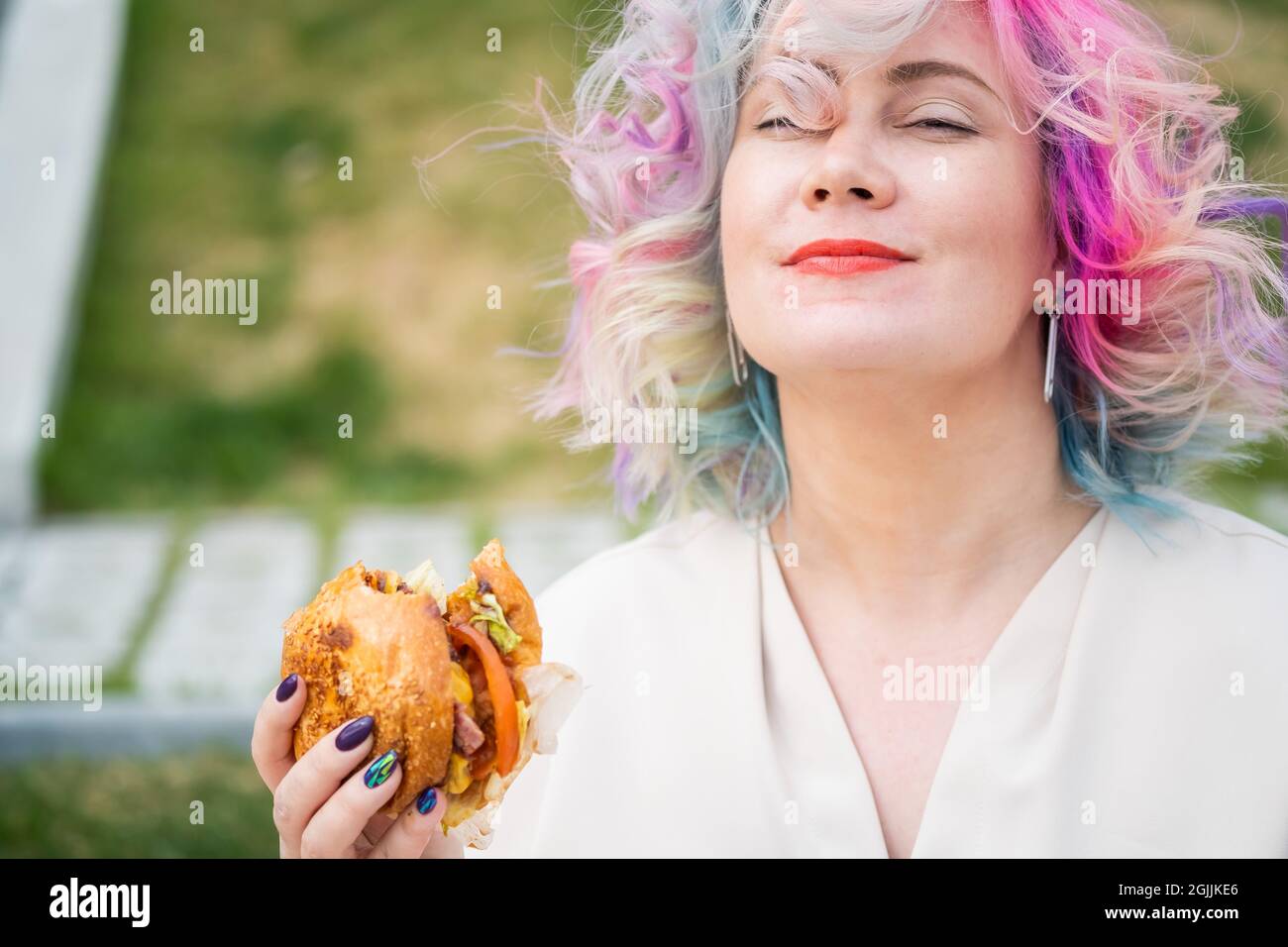 Caucasian woman with curly colored hair eating burger. Bad eating ...