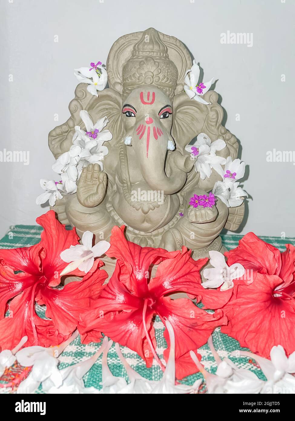 Lord Ganesh idol made of mud and decorated with white and red flowers ...