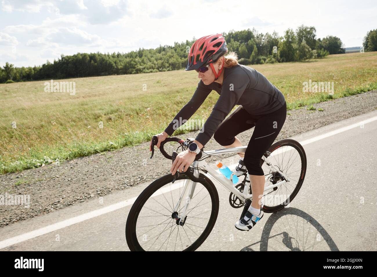 Female cyclist in sports clothing and in helmet riding a racing bike on ...
