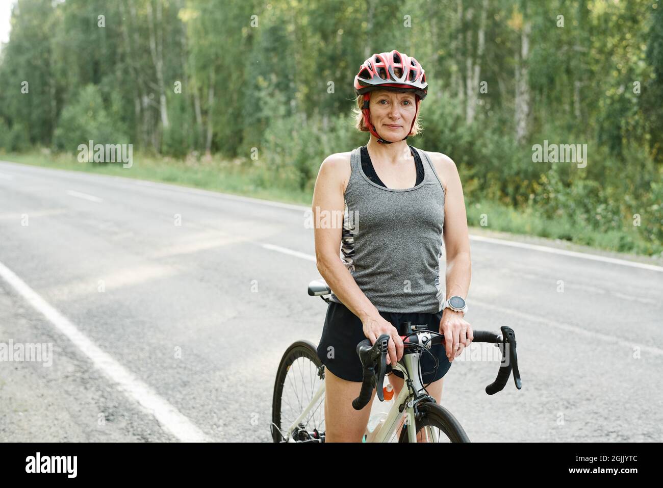 Portrait of mature woman in helmet standing with sport bike and looking at camera she taking ...