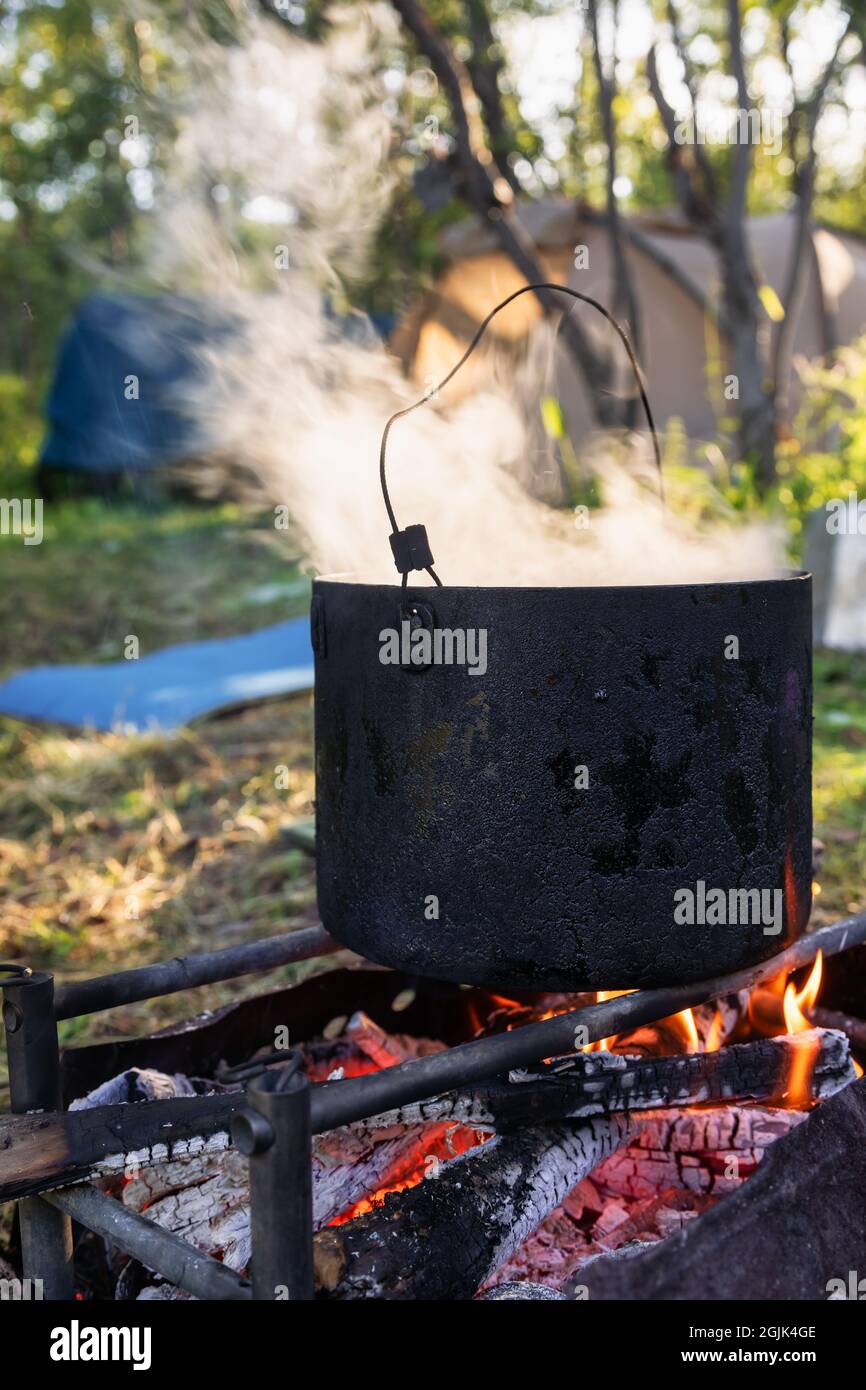 Steaming camping pot on burning campfire with cooking meal. Tents a ...