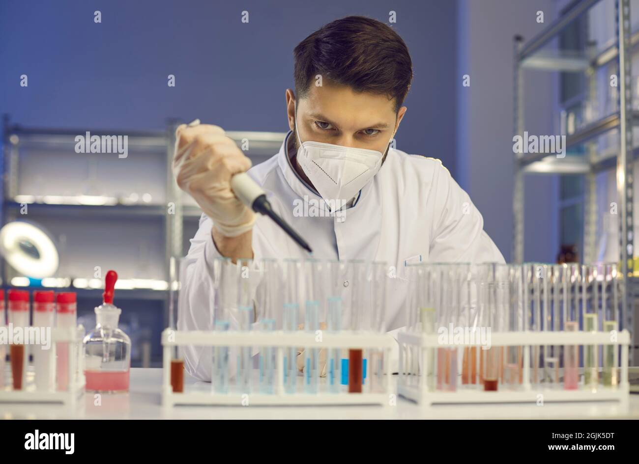 Serious and focused male scientist using a pipette to add liquid to one ...