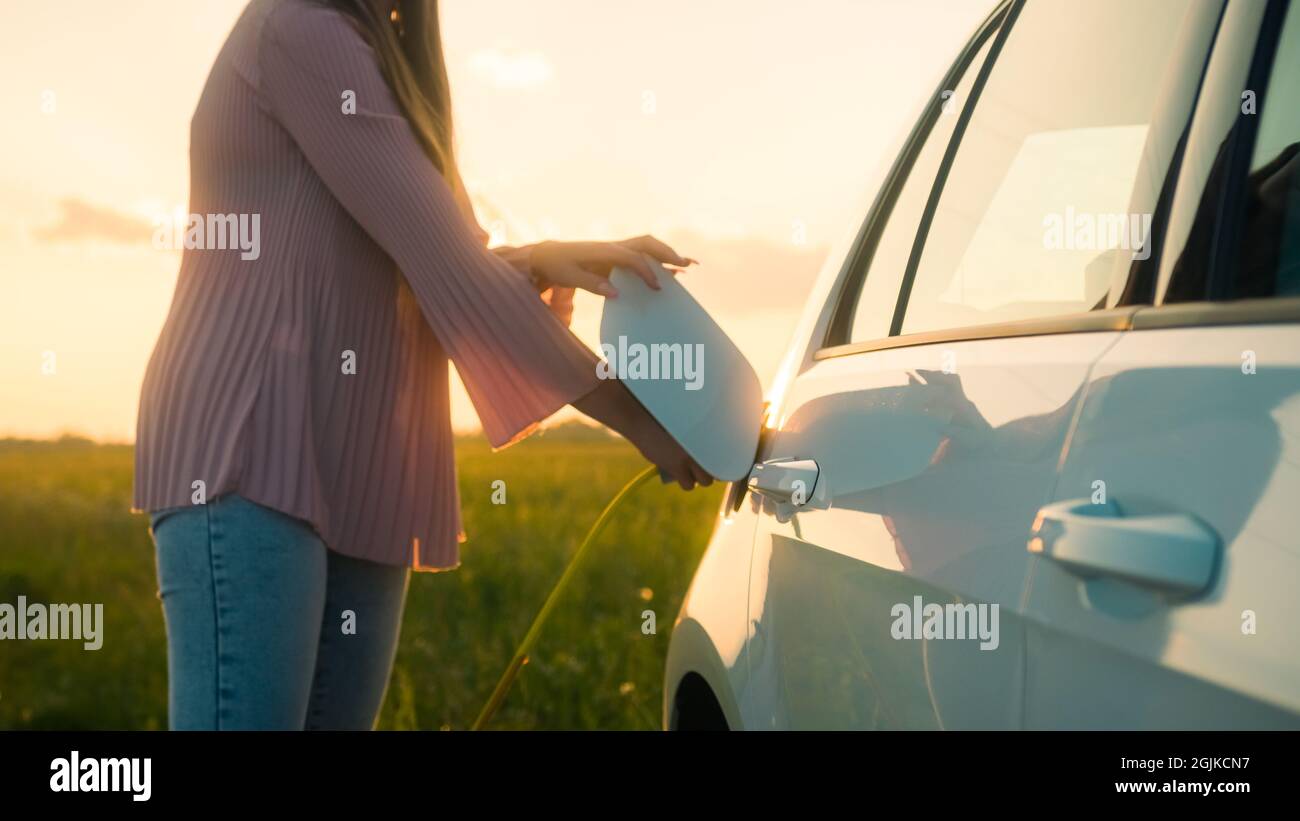 Woman charging a white electric car at a charging station near a ...
