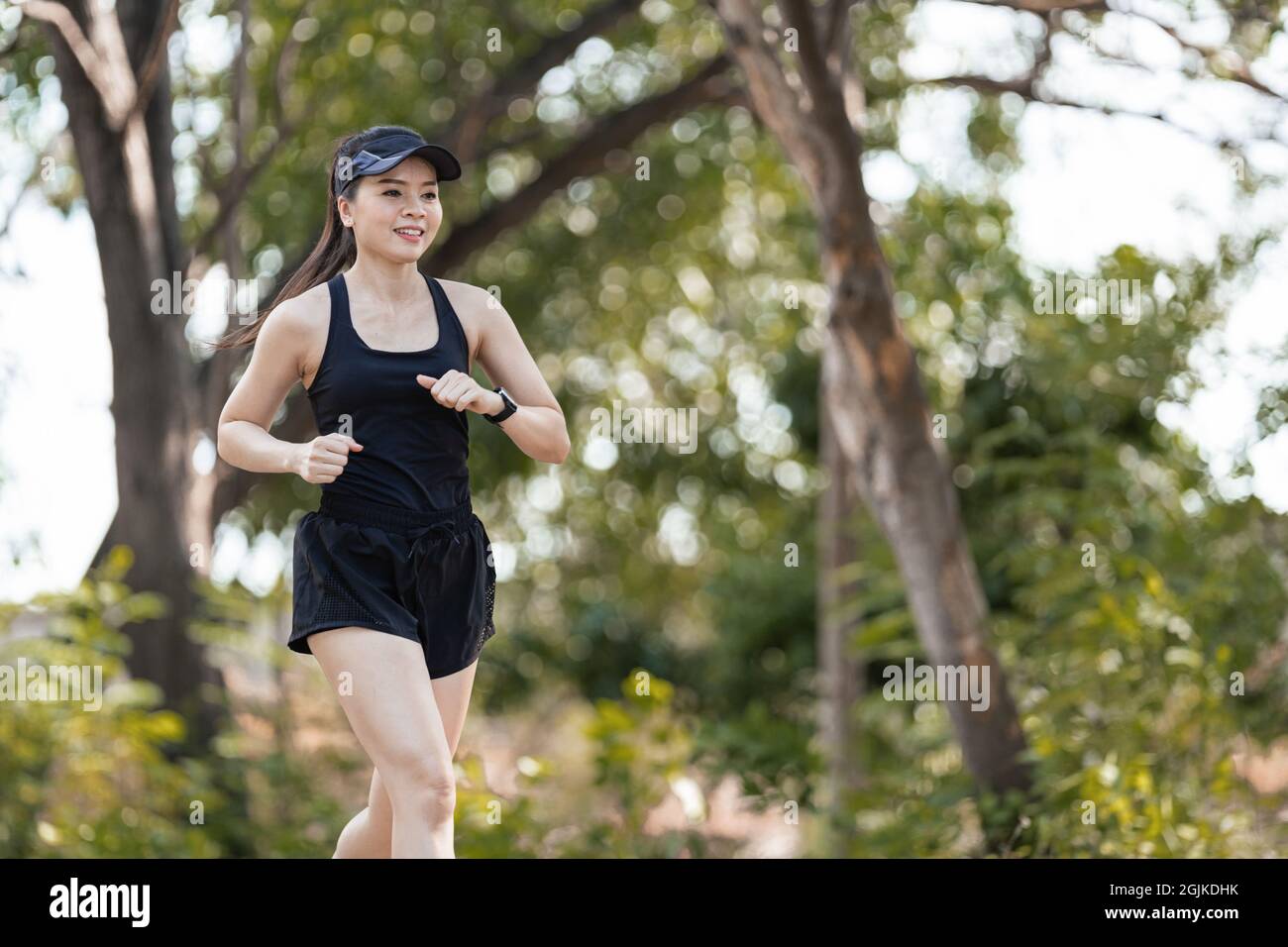 Healthy happy Asian runner in a black outfit jogging in a park during ...