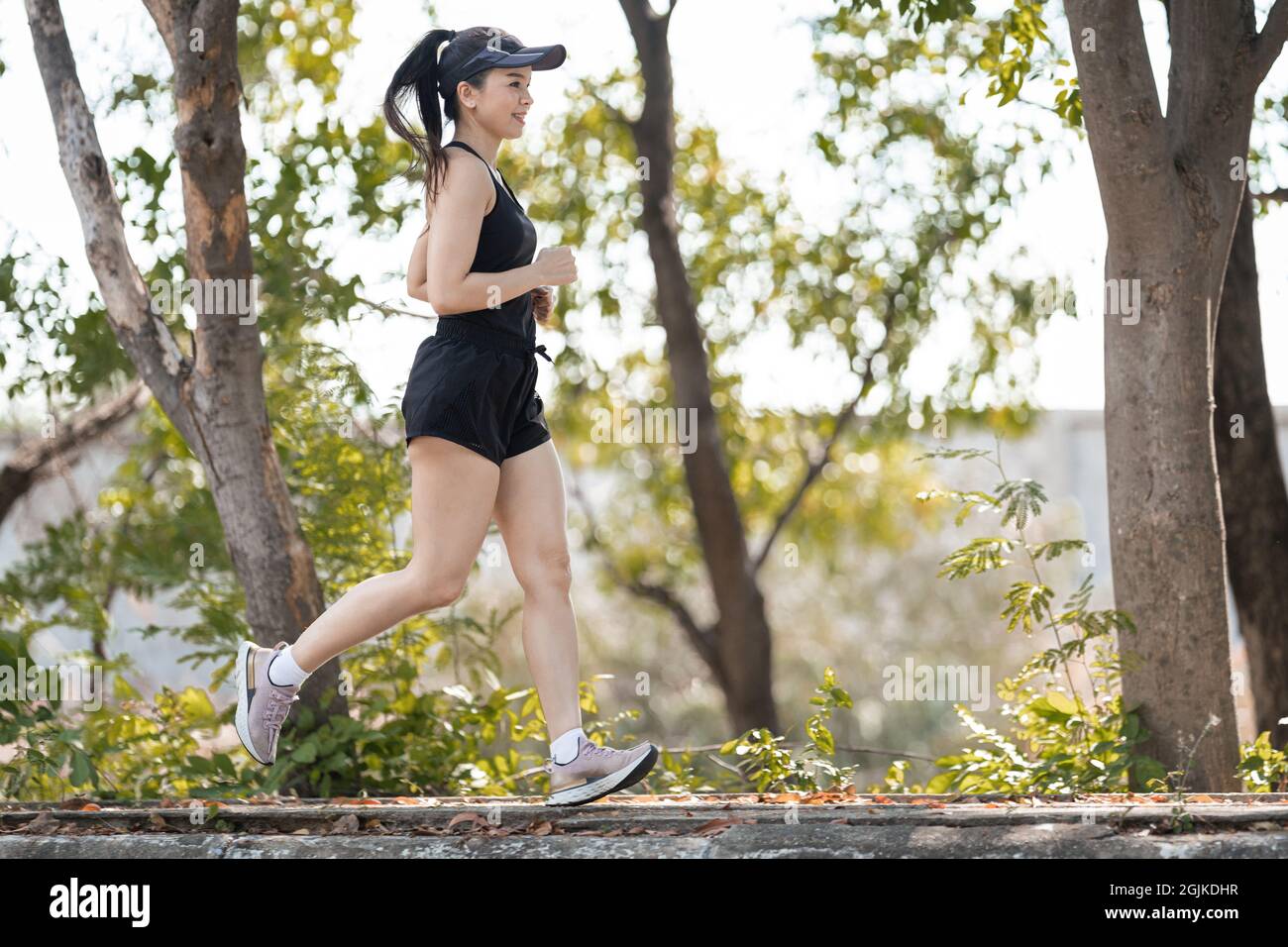 Healthy happy Asian runner in a black outfit jogging in a park during ...
