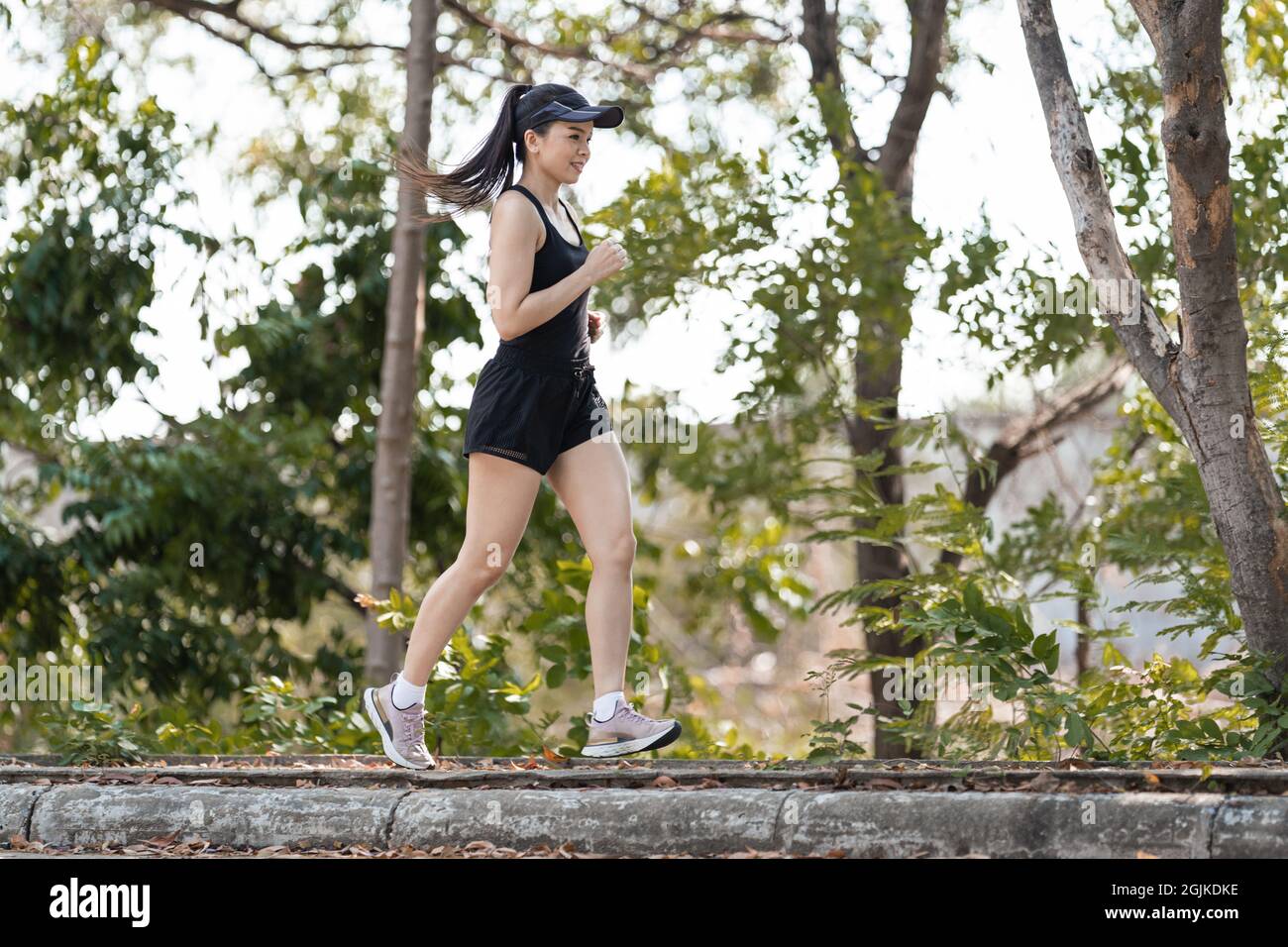 Healthy happy Asian runner in a black outfit jogging in a park during ...