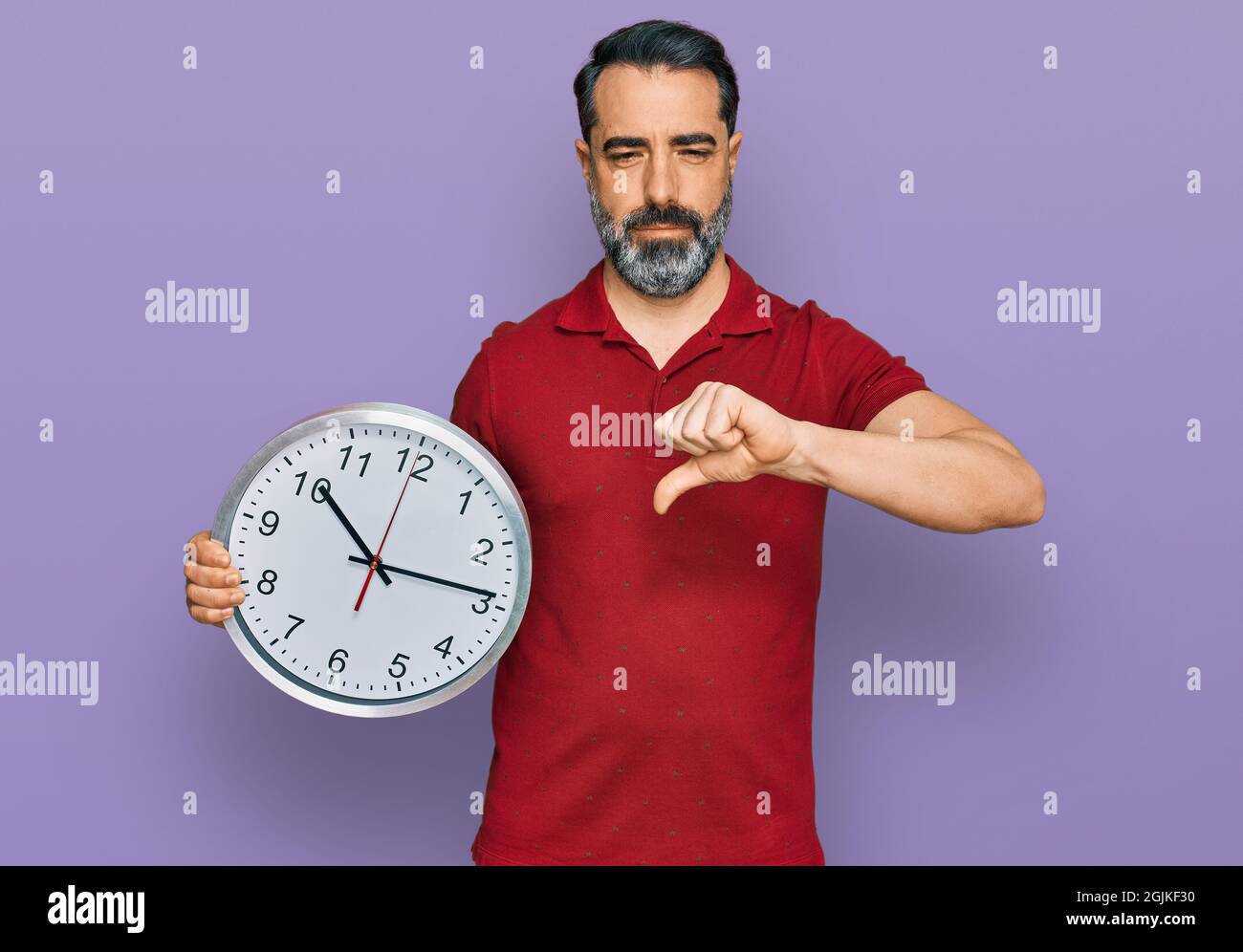Middle aged man with beard holding big clock with angry face, negative ...