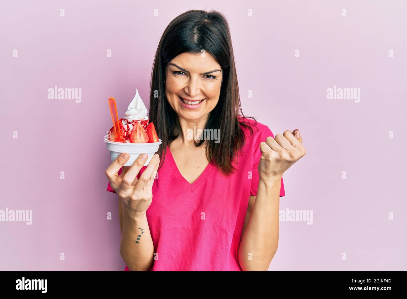 Young hispanic woman eating strawberry ice cream screaming proud ...