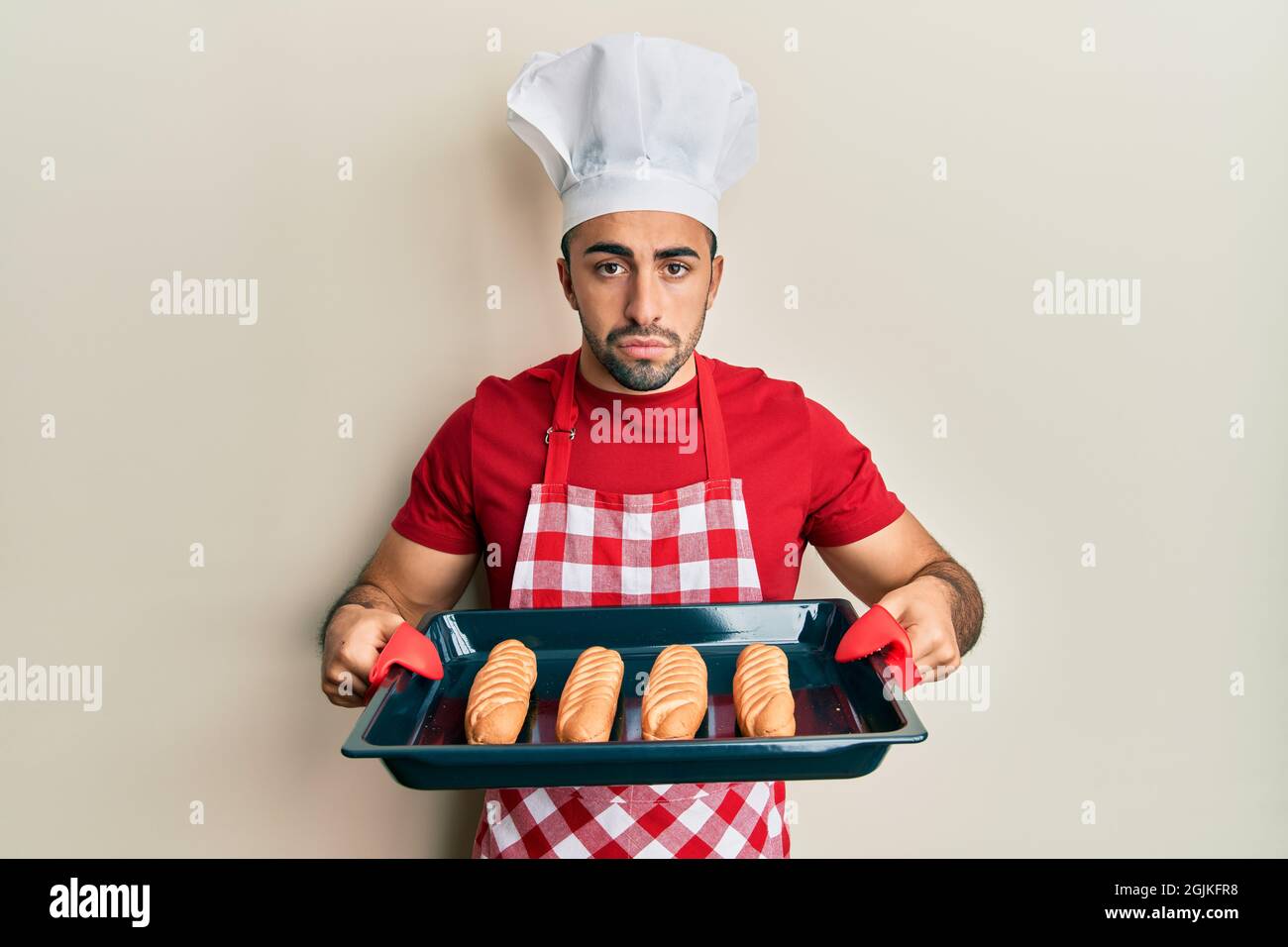 Young hispanic man wearing baker uniform holding homemade bread ...