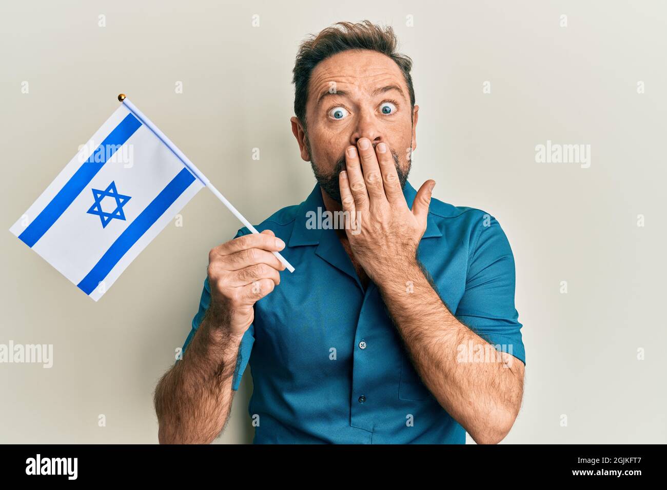 Middle age man holding israel flag covering mouth with hand, shocked ...