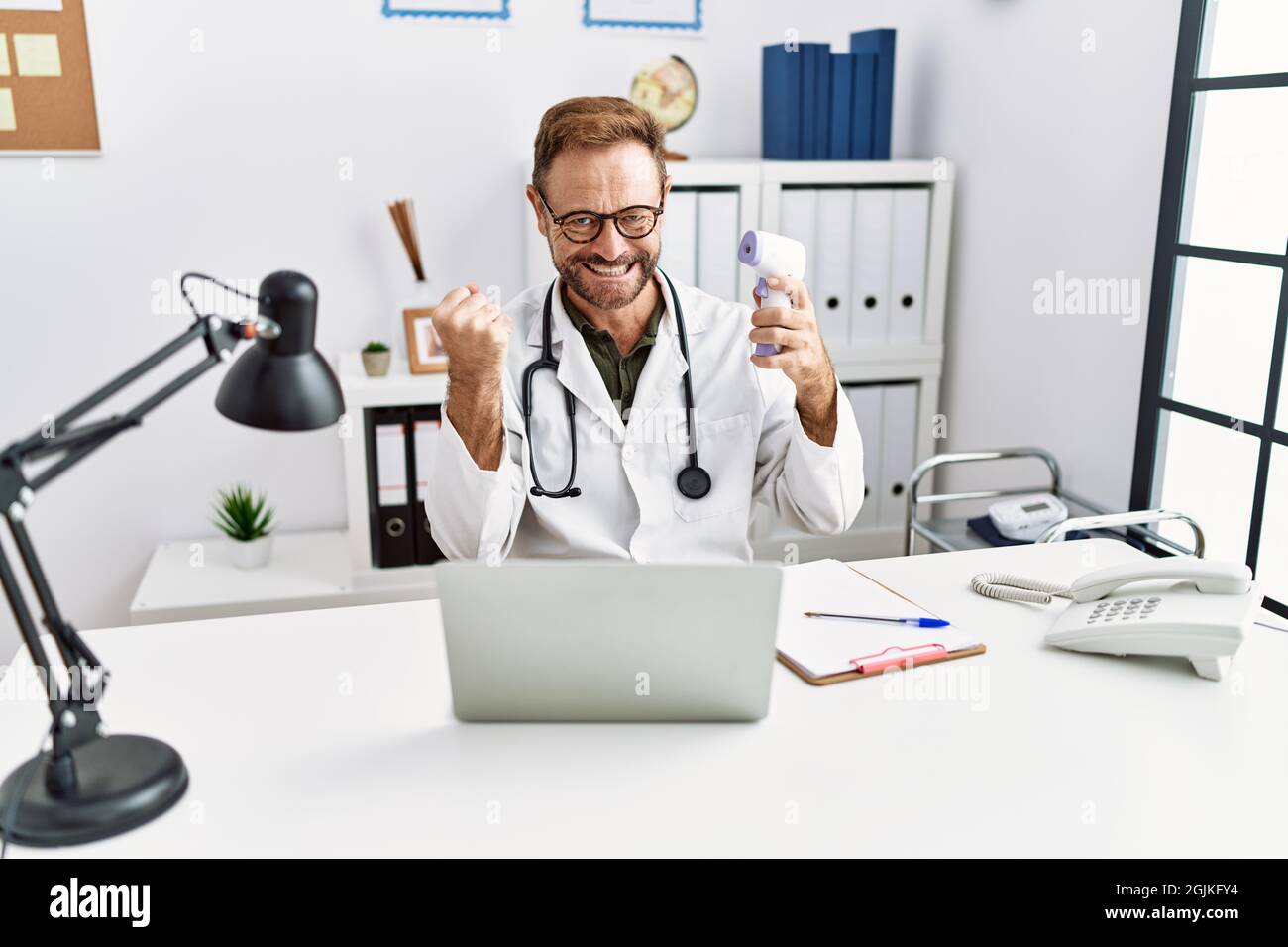 Middle age doctor man holding thermometer at the clinic screaming proud ...