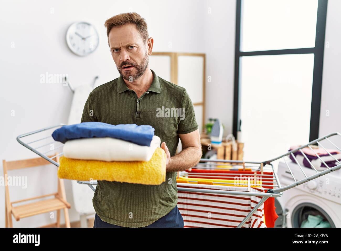 Middle age man holding folded laundry after ironing in shock face ...