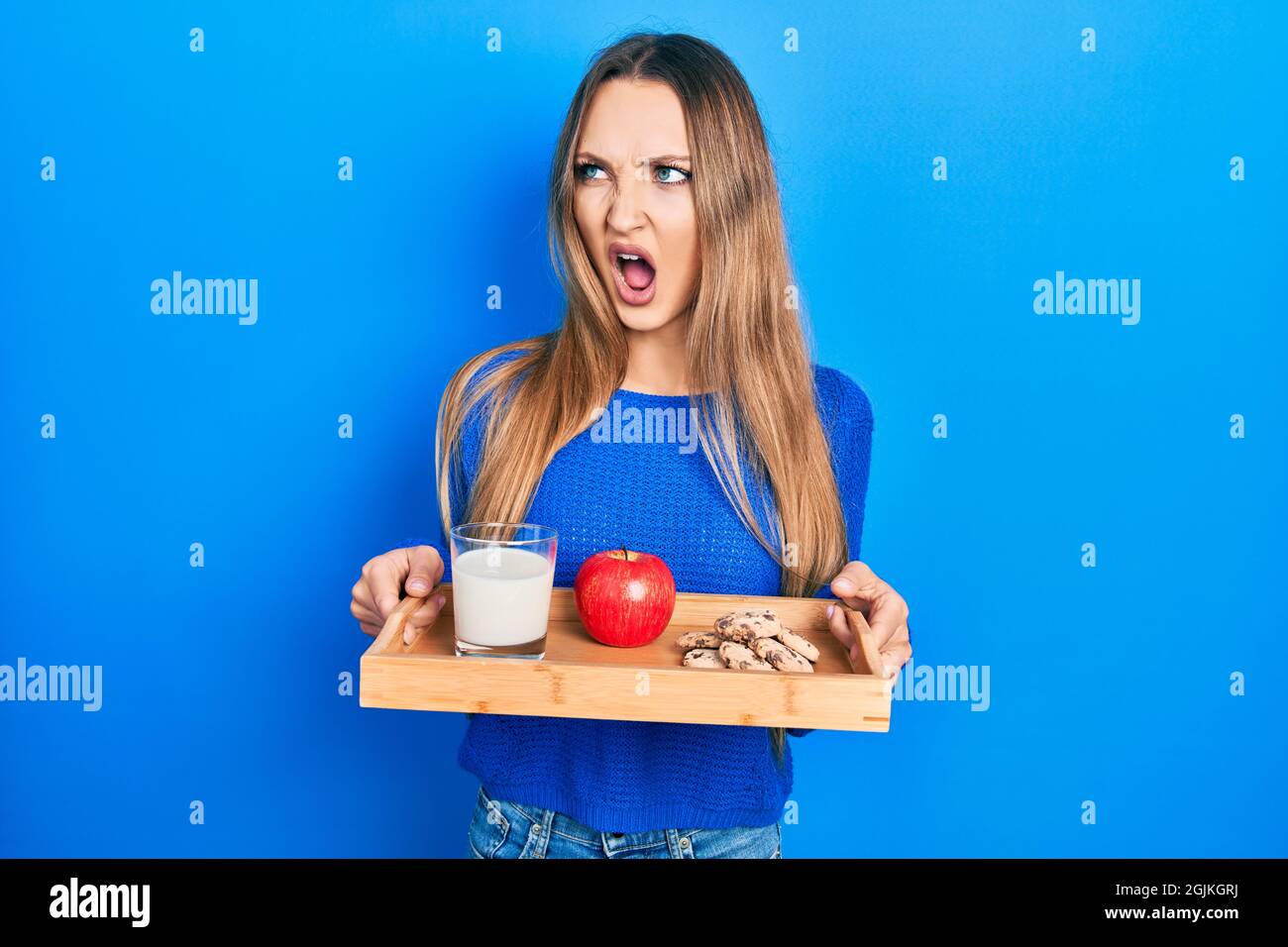 Young blonde girl holding tray with breakfast food angry and mad ...