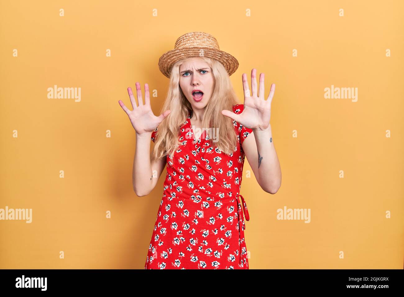 Beautiful caucasian woman with blond hair wearing summer hat afraid and ...
