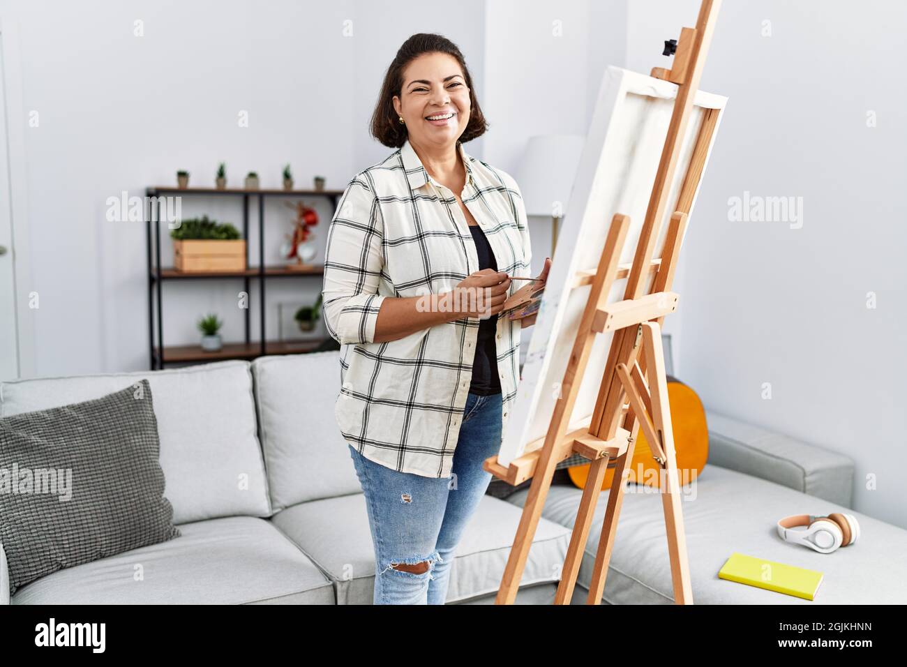 Middle age hispanic woman drawing by painter easel stand at home ...