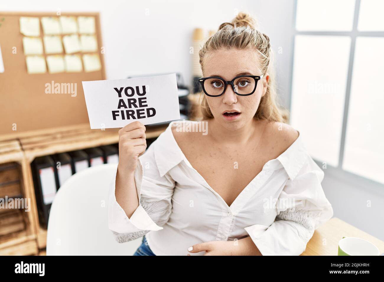 Young caucasian woman holding you are fired banner at the office scared ...