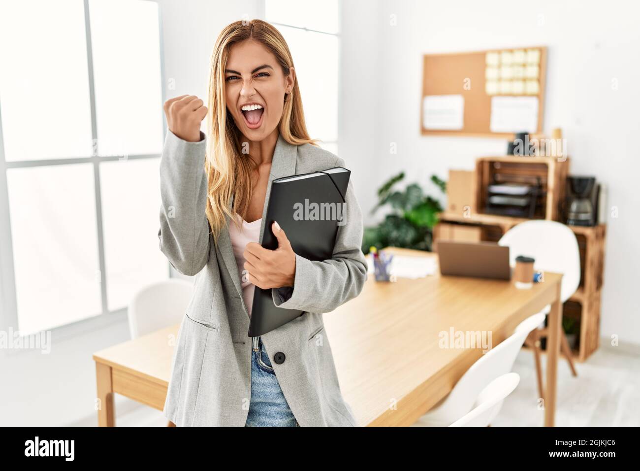Blonde business woman at the office angry and mad raising fist ...