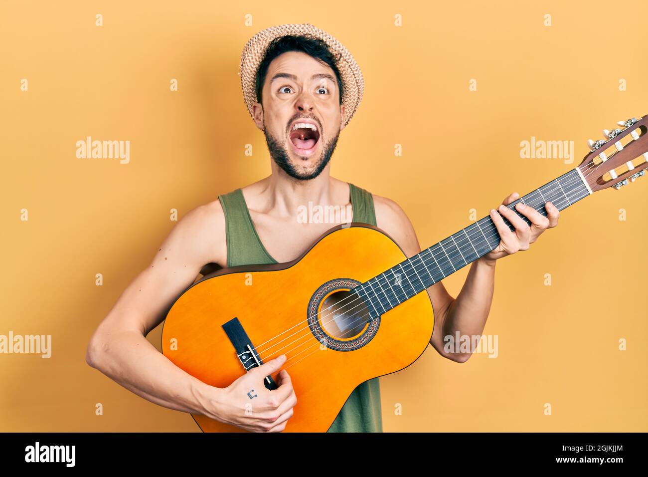 Young hispanic man playing classical guitar angry and mad screaming ...