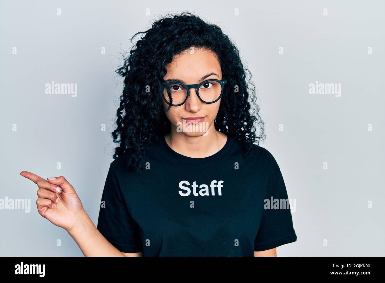 Young hispanic woman with curly hair wearing staff t shirt pointing ...