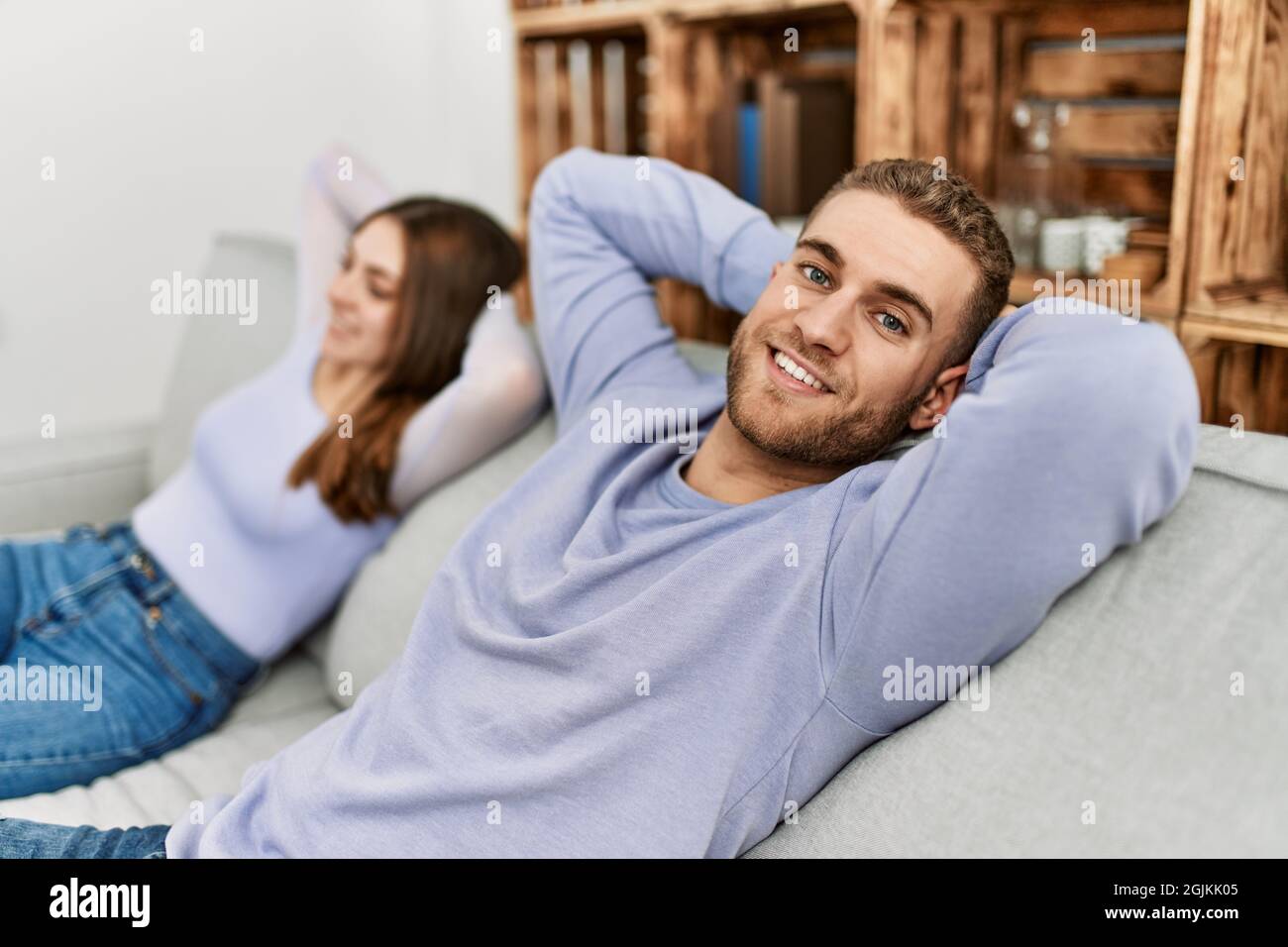 Young caucasian couple resting with hands on head sitting on the sofa ...
