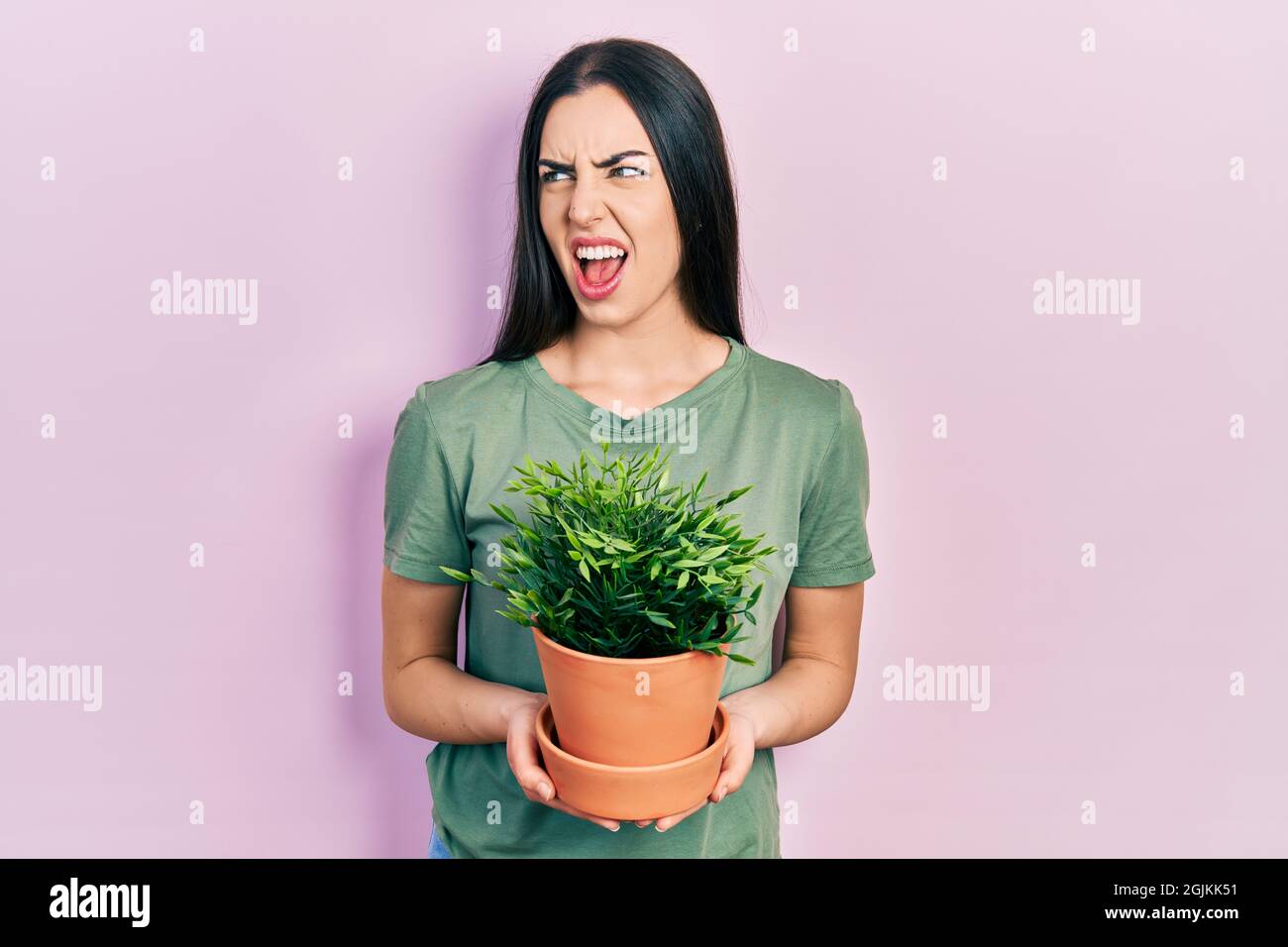 Beautiful woman with blue eyes holding green plant pot angry and mad ...