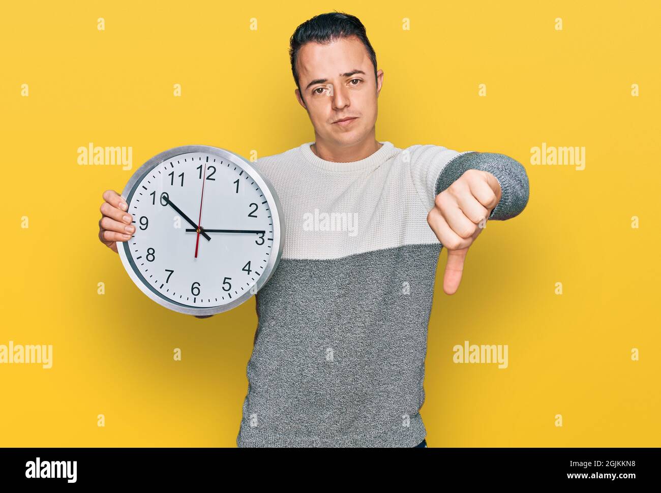 Handsome young man holding big clock with angry face, negative sign ...