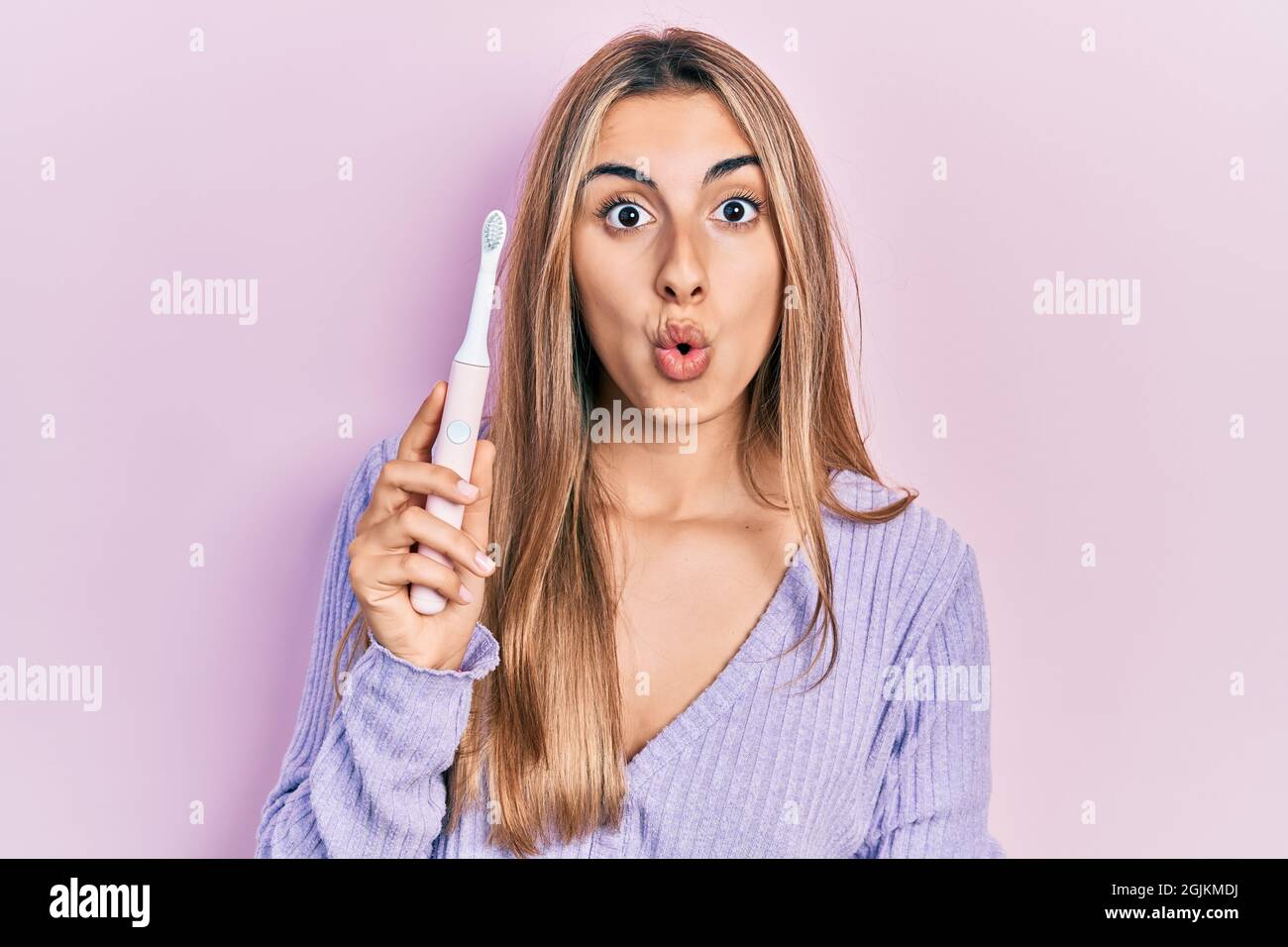 Beautiful hispanic woman holding electric toothbrush scared and amazed ...