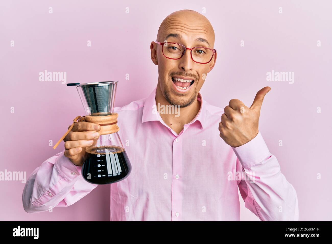 Bald man with beard holding coffee maker with filter pointing thumb up ...