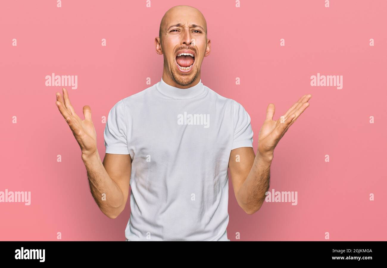 Bald man with beard wearing casual white t shirt crazy and mad shouting ...