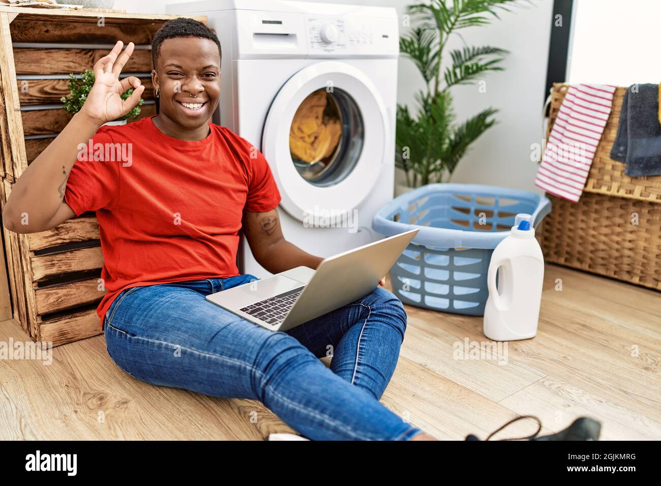 Young african man doing laundry and using computer smiling positive ...
